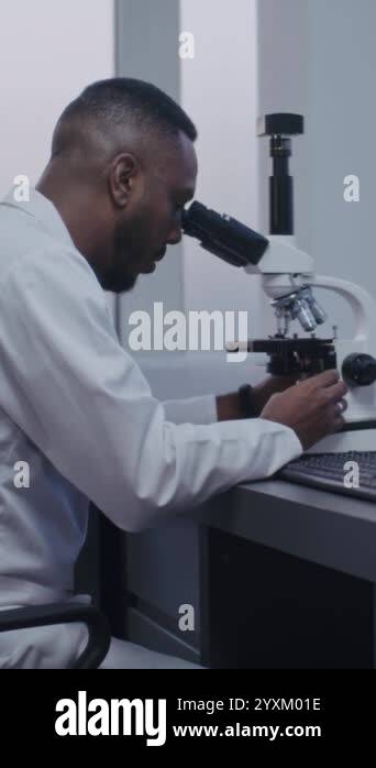 Vertical shot African American microbiologist looks under microscope ...