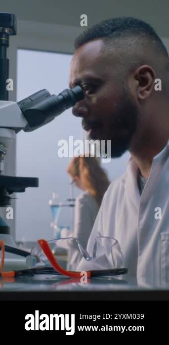 African American male microbiologist or chemist in white coat examines ...