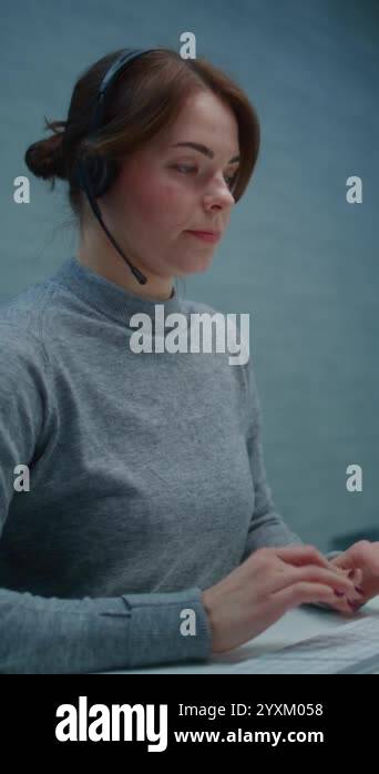 Call center office at night: Serious female technical support specialist in headset monitors ...