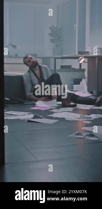 Frustrated office worker sits on the floor in destroyed office room ...