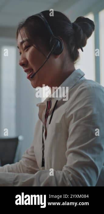 Call center office: Vertical shot of friendly Asian technical support specialist in headset ...