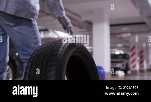 Man walks parallel to rolling tire guiding rubber with hand. Driver ...