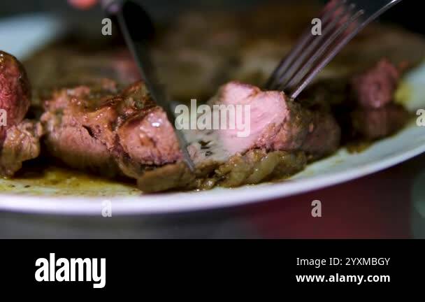 Chef slicing freshly grilled juicy beef steak meat with a knife on a ...
