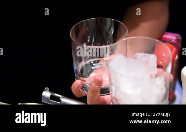 Bartender adds ice cubes into glass. slow motion, making cocktail at bar counter, Vertical ...