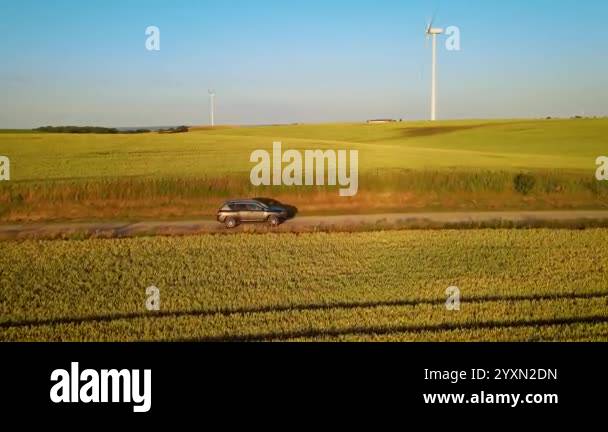 SUV driving along rural dirt road with golden wheat fields stretching ...