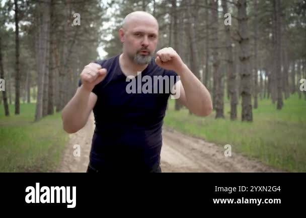 Bald male practicing boxing punches outdoors in forest path. Guy ...