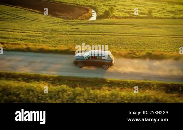 Car driving along dirt road through green fields with woman behind ...