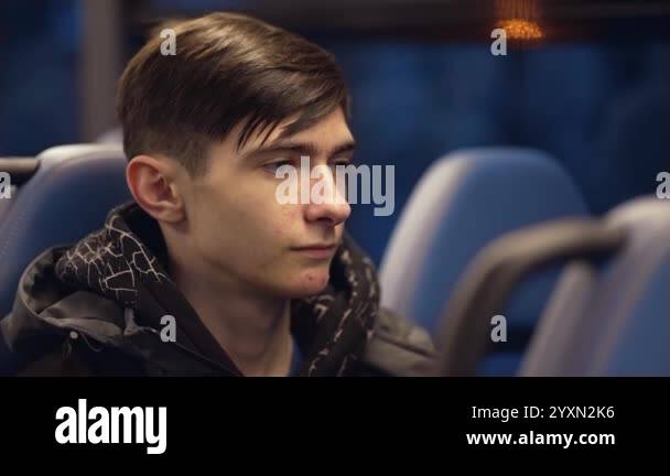 Boy sitting in bus at night, looking ahead with calm expression. Male ...