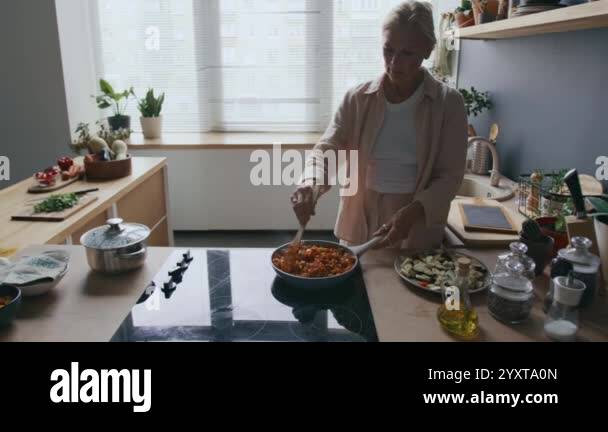 Medium shot of adult Caucasian woman finishing Bolognese sauce ...