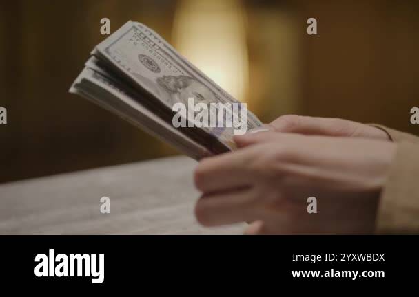 Detailed view of hands counting a stack of US dollar bills on a table ...
