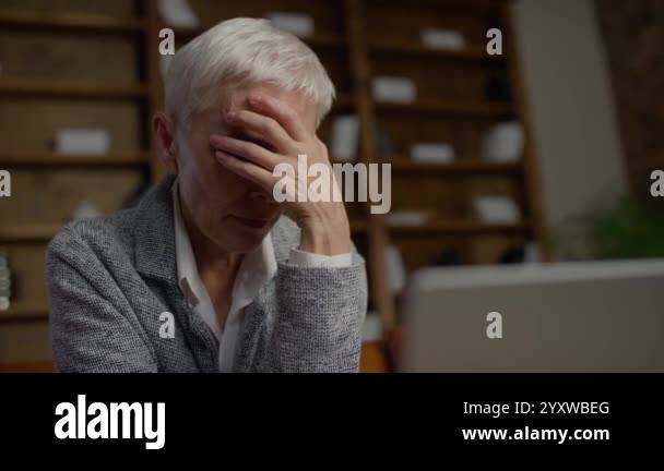 Elderly woman in distress covering her face with one hand, seated at a ...