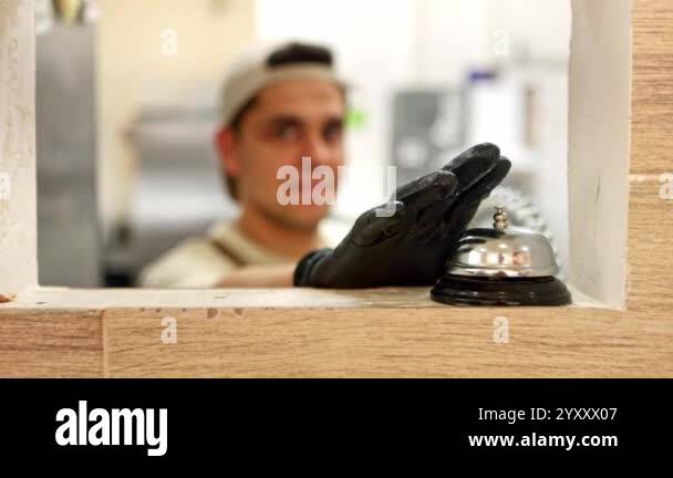 A baker wearing a cap and a black glove rings a service bell in a ...