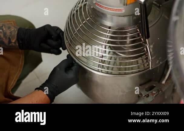 Close-up of a chef wearing black gloves, adjusting a metal safety guard ...