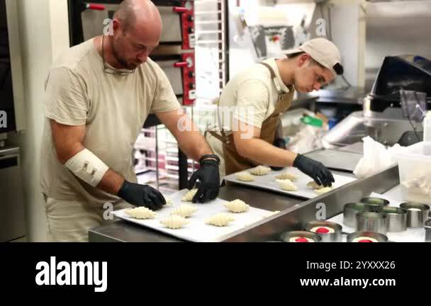 Two bakers work together meticulously shaping croissants on a stainless ...