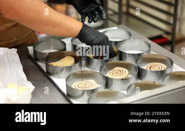 A baker places cinnamon rolls dough into round steel baking rings ...