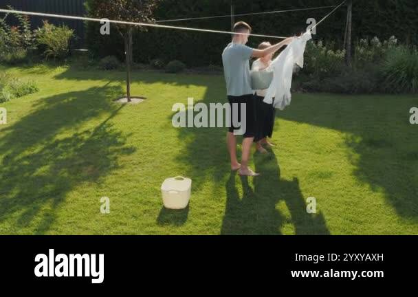 Two people hang laundry on a clothesline in a sunny backyard ...