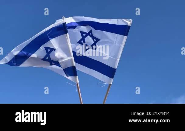 Two Israeli flags waving in the wind against a bright, clear blue sky ...