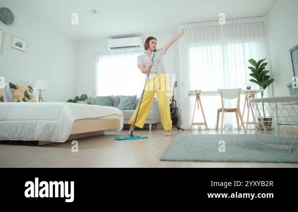 Caucasian housekeeper mopping the floor while dancing in lively mood at modern apartment. Happy ...