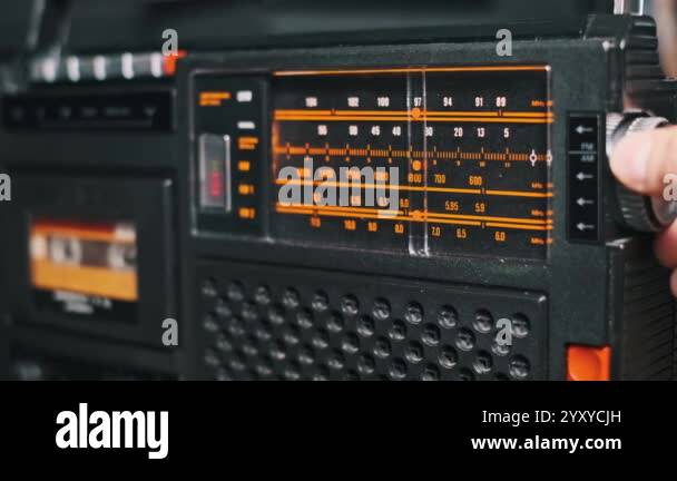 Hand turning the knob of a vintage radio, seeking an FM station. The ...