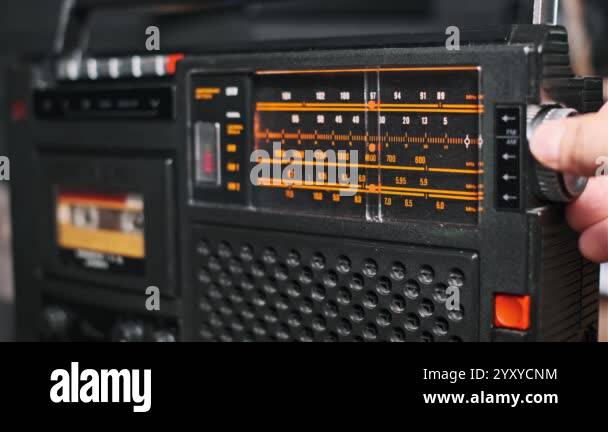 Close-up of a hand tuning an analog dial on a vintage radio with a ...
