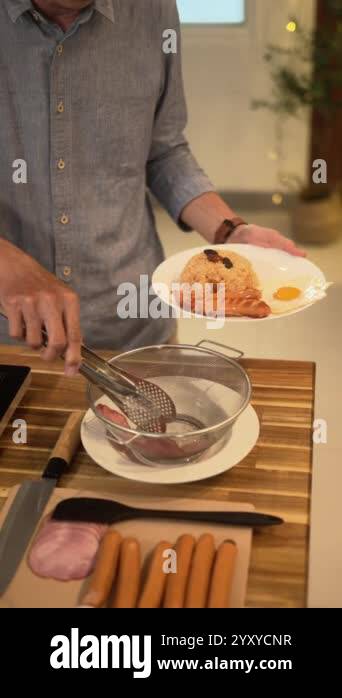 Man plating a breakfast dish featuring fried rice, grilled sausages and ...