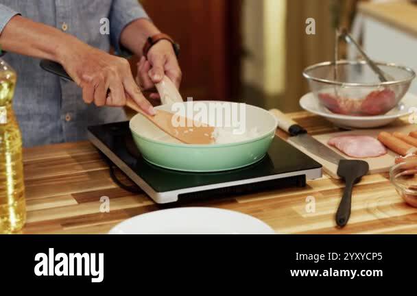 Man stirring ingredients in frying pan on an induction stove, preparing ...