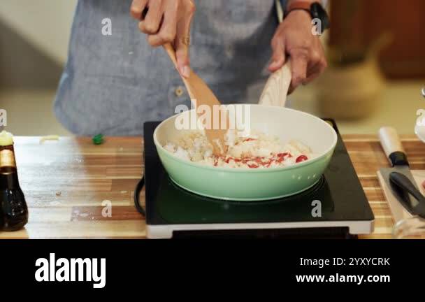 Close up of man stirring fried rice in green pan using a wooden spatula ...