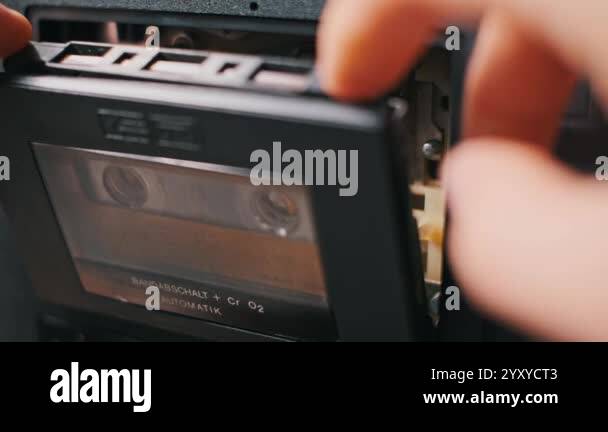 A hand inserts a used audio cassette into a vintage tape player. The ...