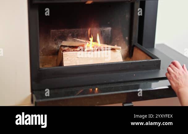 Person adding kindling to flames inside modern fireplace to build up ...