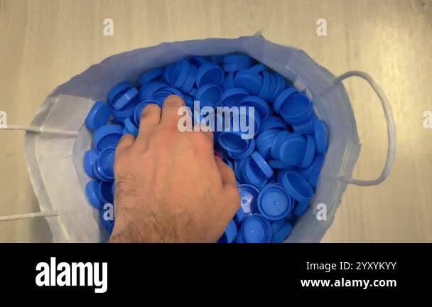 Dozens of plastic blue caps from a water bottle in a cardboard bag are ...