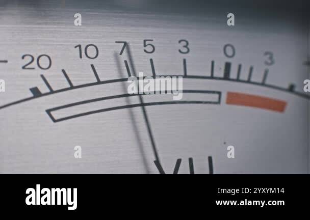 Close-up of a VU meter needle fluctuating on a brushed metal scale ...