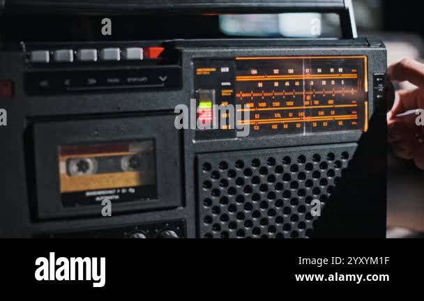 A hand tunes a vintage radio dial illuminated by a warm yellow ...