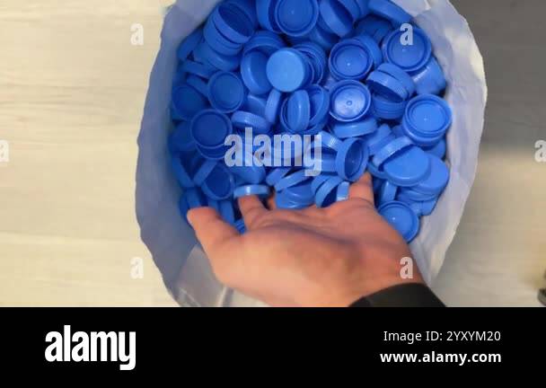 Dozens of plastic blue caps from a water bottle in a cardboard bag are ...