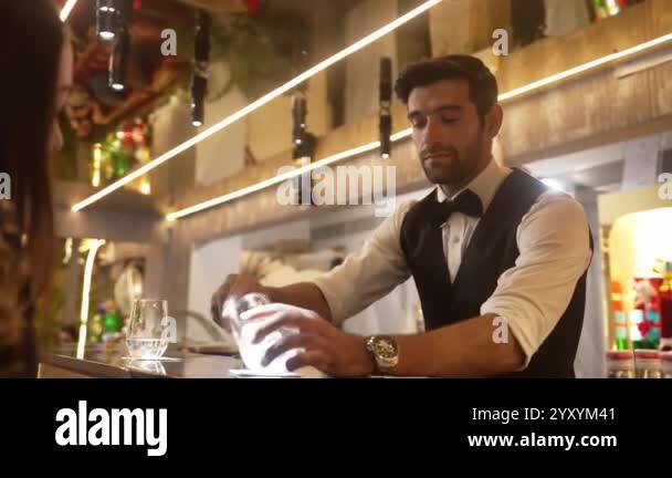 Focusing on smart bartender serving gin fizz or tonic at luxurious bar while engaging lively ...