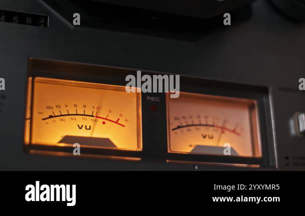 A close-up view of a vintage VU meter illuminated by a warm amber light ...