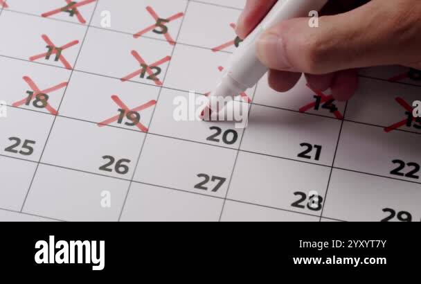 Hand marking off days on a calendar with a red marker, signifying the ...