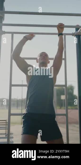 A young athlete exercises on monkey bars in an outdoor fitness park ...