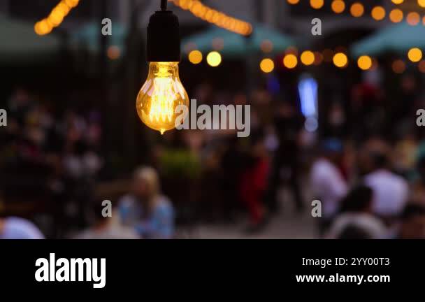 A glowing light bulb in the foreground. In the blurred background, a ...