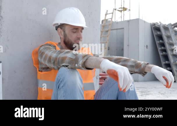 Builder repairman, foreman in safety helmet and vest sitting down to ...