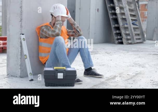 Builder repairman, foreman in safety helmet and vest sitting down to ...
