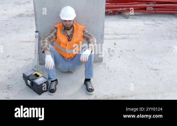 Builder repairman, foreman in safety helmet and vest sitting down to ...