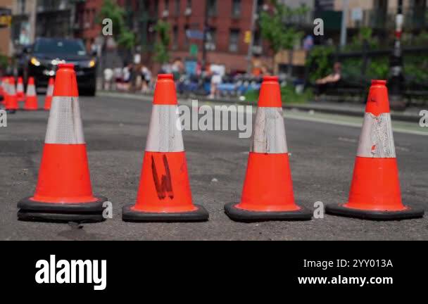 Bright orange traffic cones are lined up along a busy city street ...