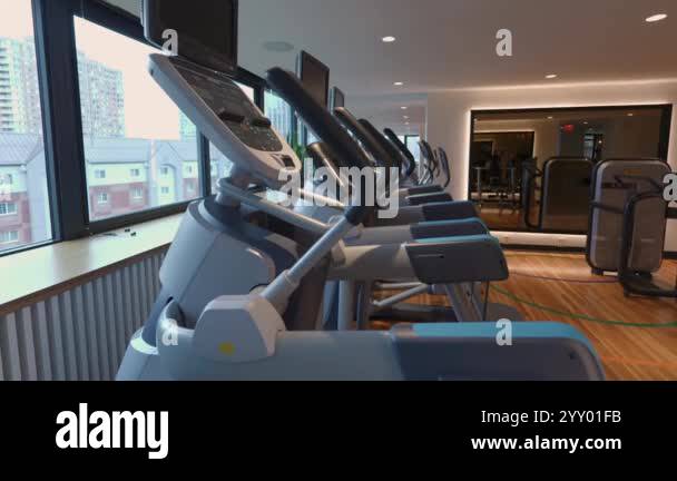 A row of modern, sleek treadmills is set up in a contemporary gym that ...