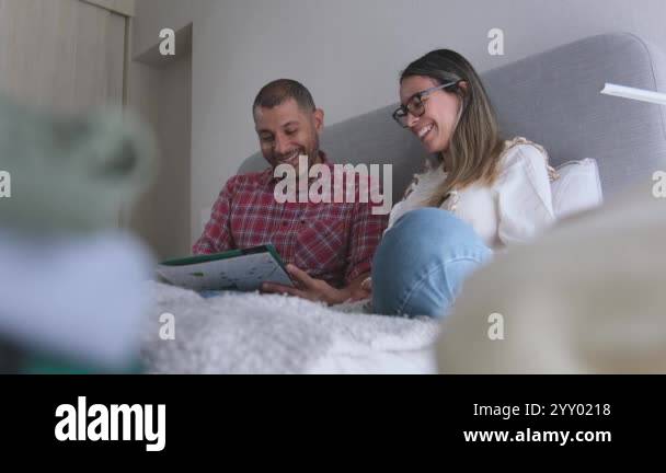 A man and woman are sitting on a bed with a magazine open in front of ...