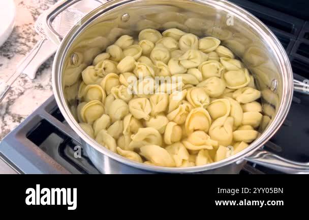 A pot filled with boiling water and pasta shells sits on a gas stove ...