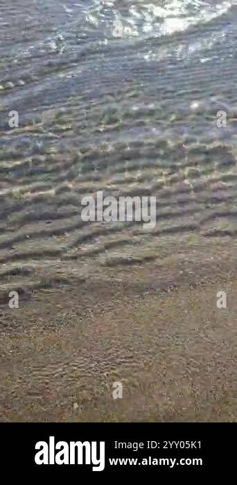 Small waves of clean transparent water rolling onto sand of shore on ...