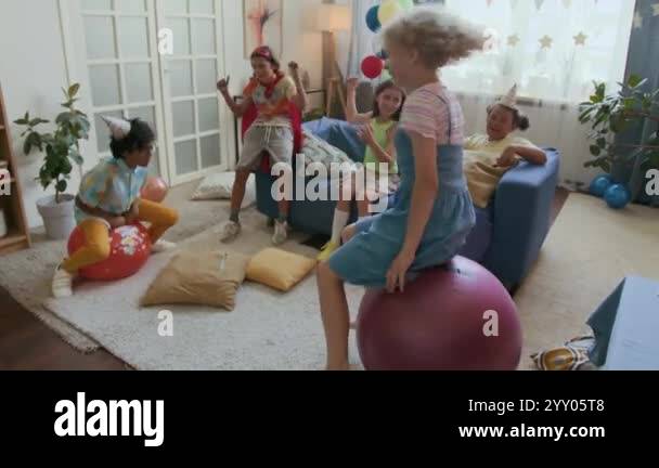 Birthday boy and his girl friend jumping on hopper balls while celebrating with company of gen ...