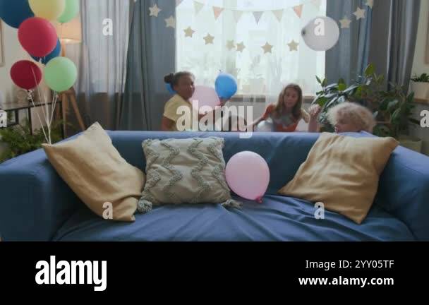 Tilt up view of five children popping up from behind sofa throwing ...