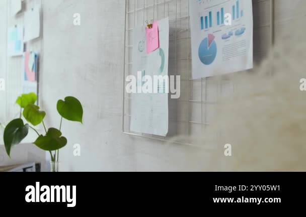 No people shot of wire mesh bulletin board with several printed paper charts and graphs on wall ...