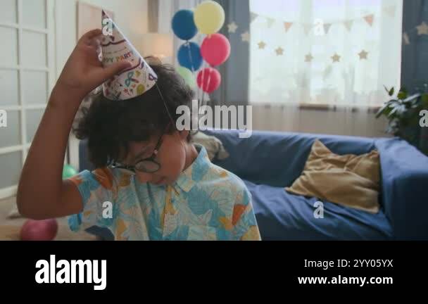 Portrait of gen alpha boy with glasses putting on party hat and smiling ...